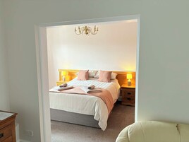 Quarto com cama, luminárias de cabeceira, candelabro e mesa de cabeceira de madeira.