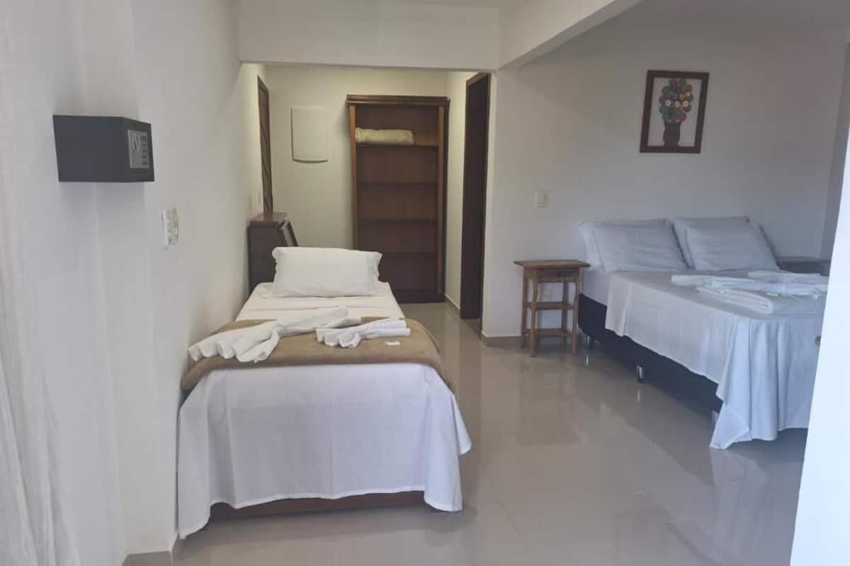 Quarto de hotel com duas camas, um guarda-roupa, uma mesinha de cabeceira e um candeeiro fixo na parede.