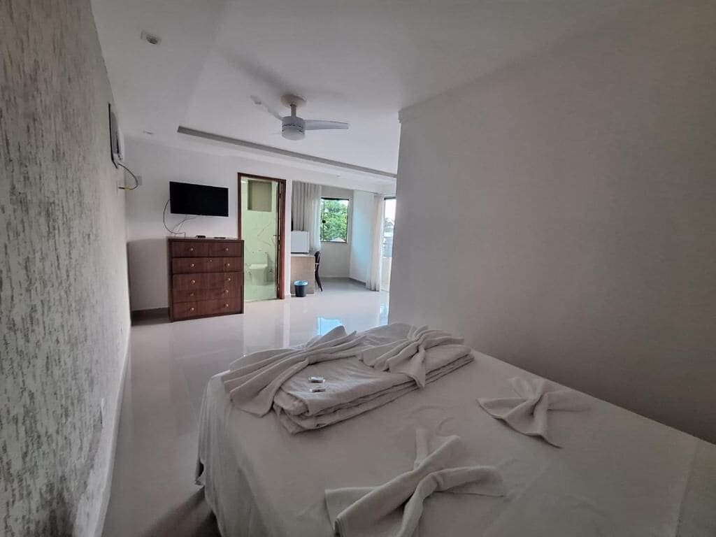 Quarto com cama, penteadeira, televisão e ventoinha no teto.