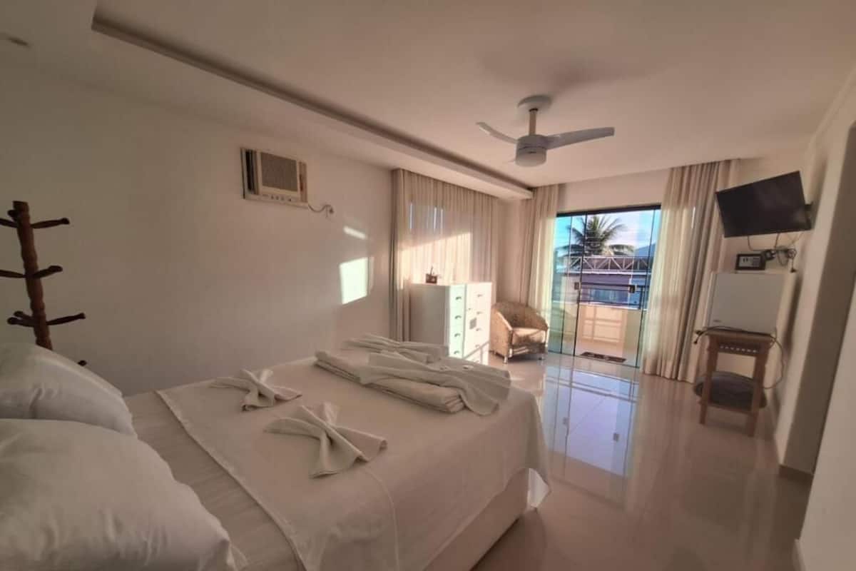 Quarto de hotel com cama, ventoinha no teto, televisão e vista para o exterior.