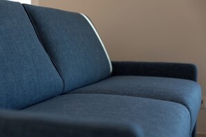 Um close-up de um sofá estofado azul escuro, com textura lisa e detalhes brancos nas bordas.