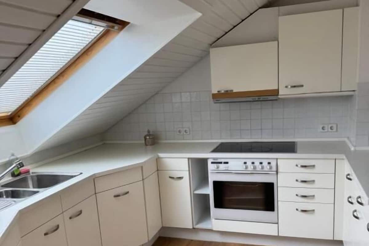Uma cozinha com armários brancos, bancada de madeira, claraboia e forno embutido.