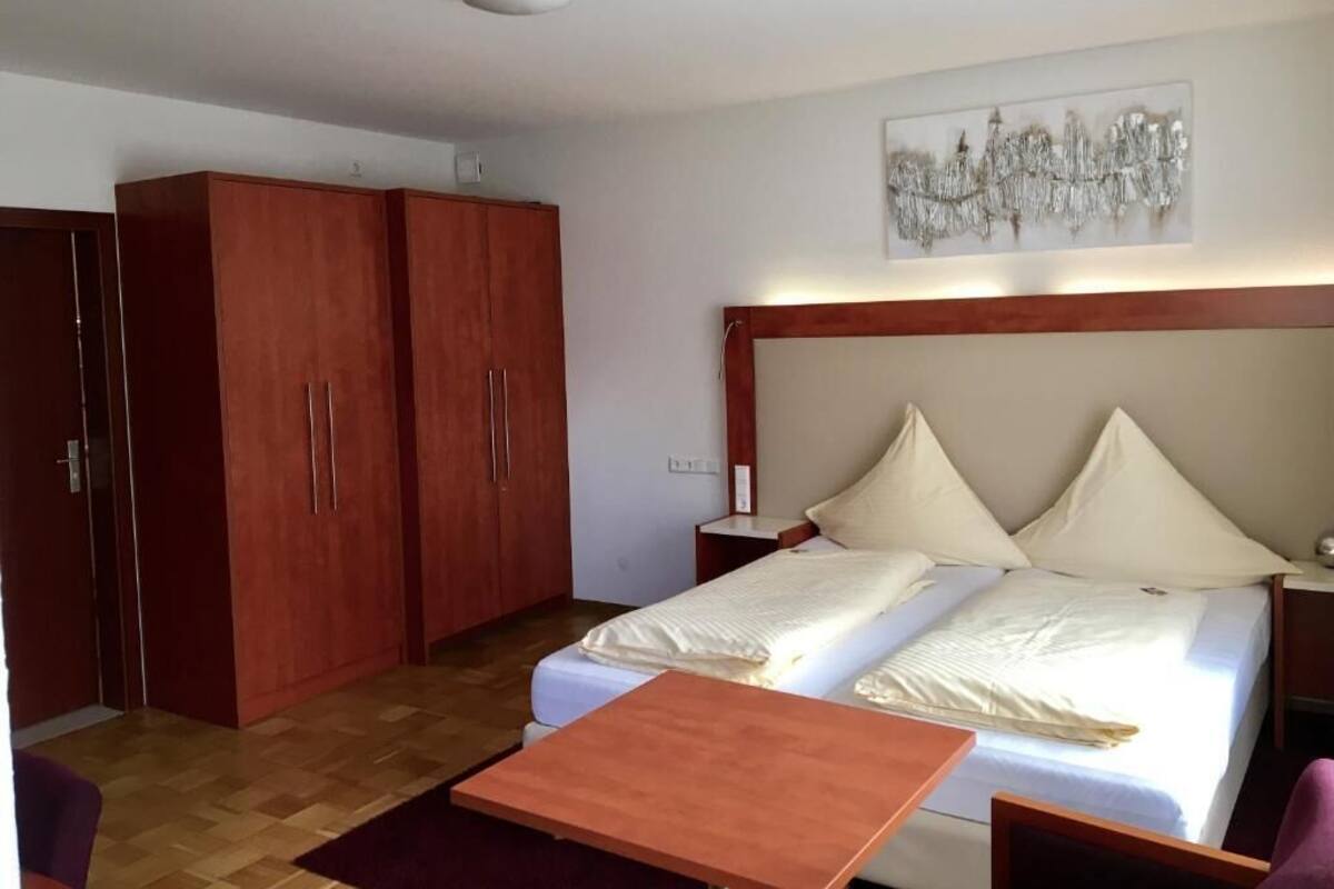 Quarto de hotel com uma cama, duas mesas de cabeceira, um guarda-roupa de madeira e um quadro na parede.