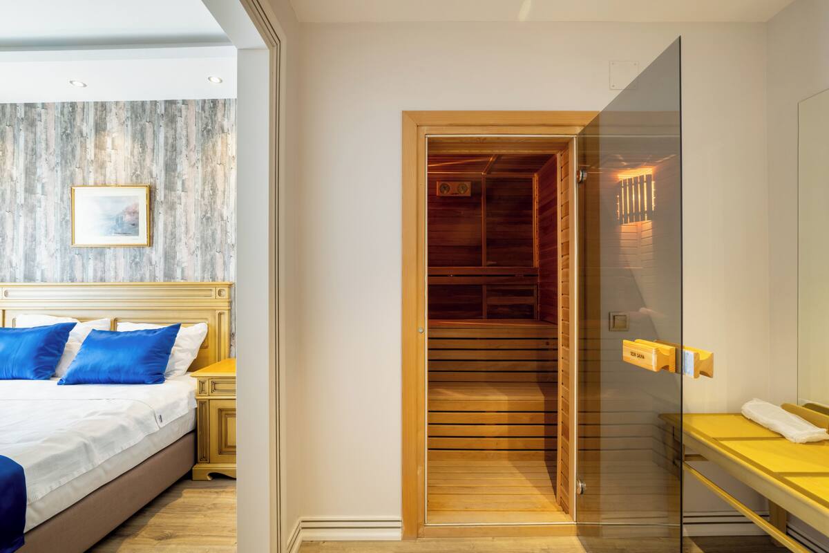 Quarto com cama, mesas de cabeceira, guarda-roupa de madeira e divisória de vidro.
