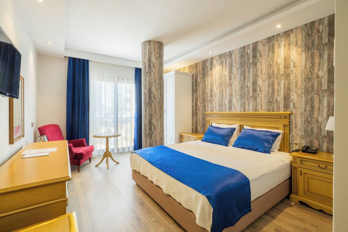 Quarto de hotel com uma cama grande, uma escrivaninha, uma cadeira, uma mesinha de apoio e um guarda-roupa.