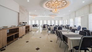 Uma sala de conferências espaçosa com uma mesa comprida, cadeiras, área de buffet e luminárias decorativas no teto.