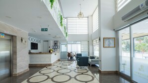 Um saguão de hotel com uma mesa de recepção, um candelabro, um relógio e uma grande janela com vista.