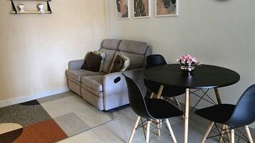Uma sala de estar com sofá, mesa de jantar com cadeiras, espelho pendurado e obras de arte nas paredes.