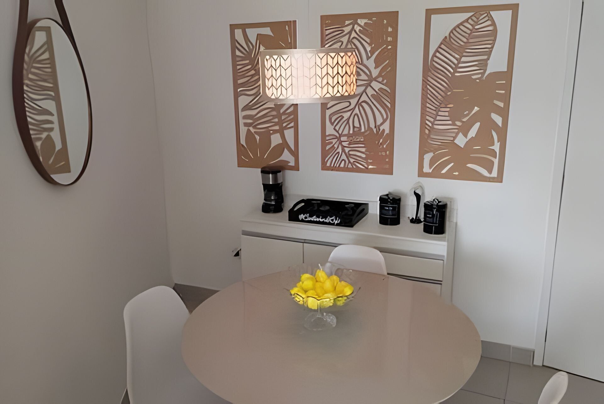 Uma sala de jantar com uma mesa redonda, cadeiras, máquina de café, chaleira e painéis decorativos na parede.