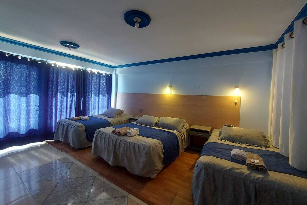 Quarto de hotel com duas camas, piso de madeira, tapete estampado e janela com cortinas.
