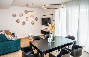 Uma sala de estar moderna com um sofá verde-água, uma mesa de jantar com cadeiras, uma TV de tela plana fixada na parede e obras de arte decorativas.