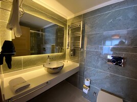 Casa de banho moderna com um espelho grande, lavatório suspenso, porta-toalhas e dispensador de toalhas.