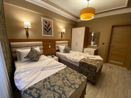 Quarto de hotel com duas camas, um guarda-roupa, mesa de cabeceira com abajur, espelho e luminária no teto.