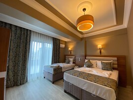 Quarto de hotel com duas camas, uma janela grande com cortinas translúcidas, luminária no teto e luminárias fixadas na parede.