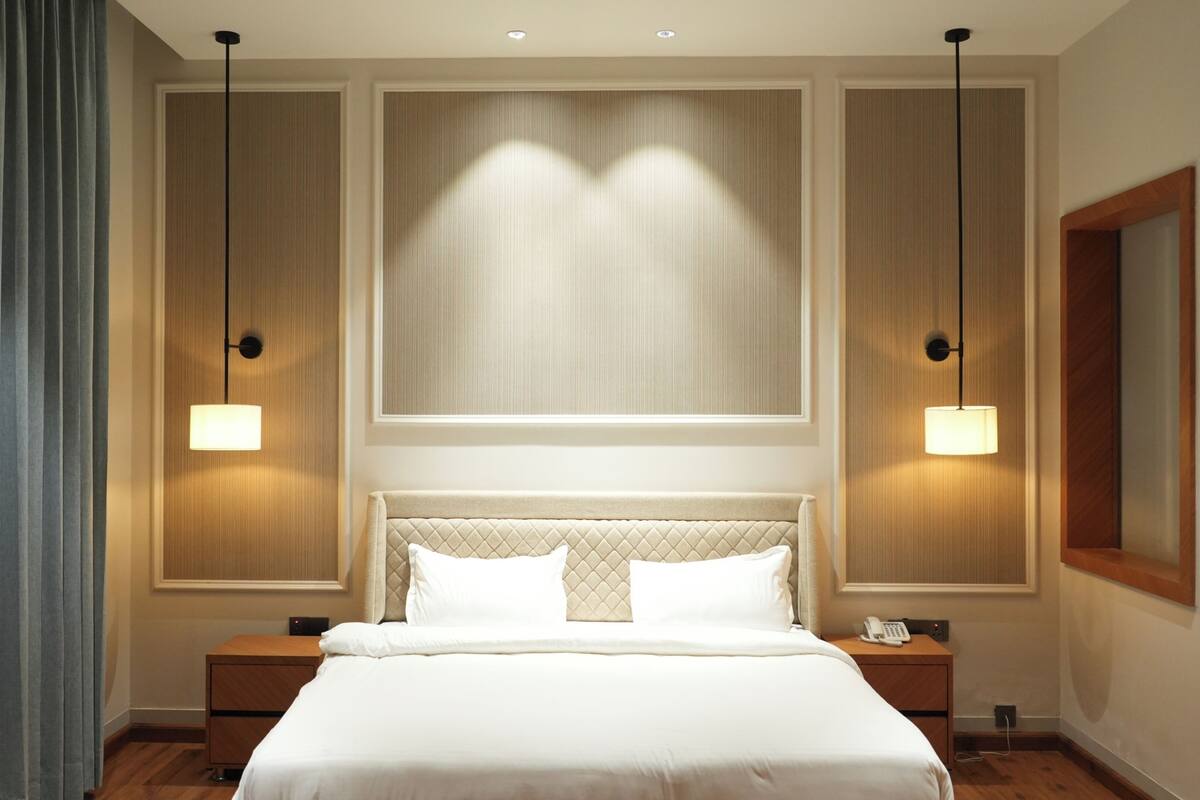 Quarto de hotel com uma cama grande, duas mesas de cabeceira, telefone fixado na parede e duas luminárias pendentes.