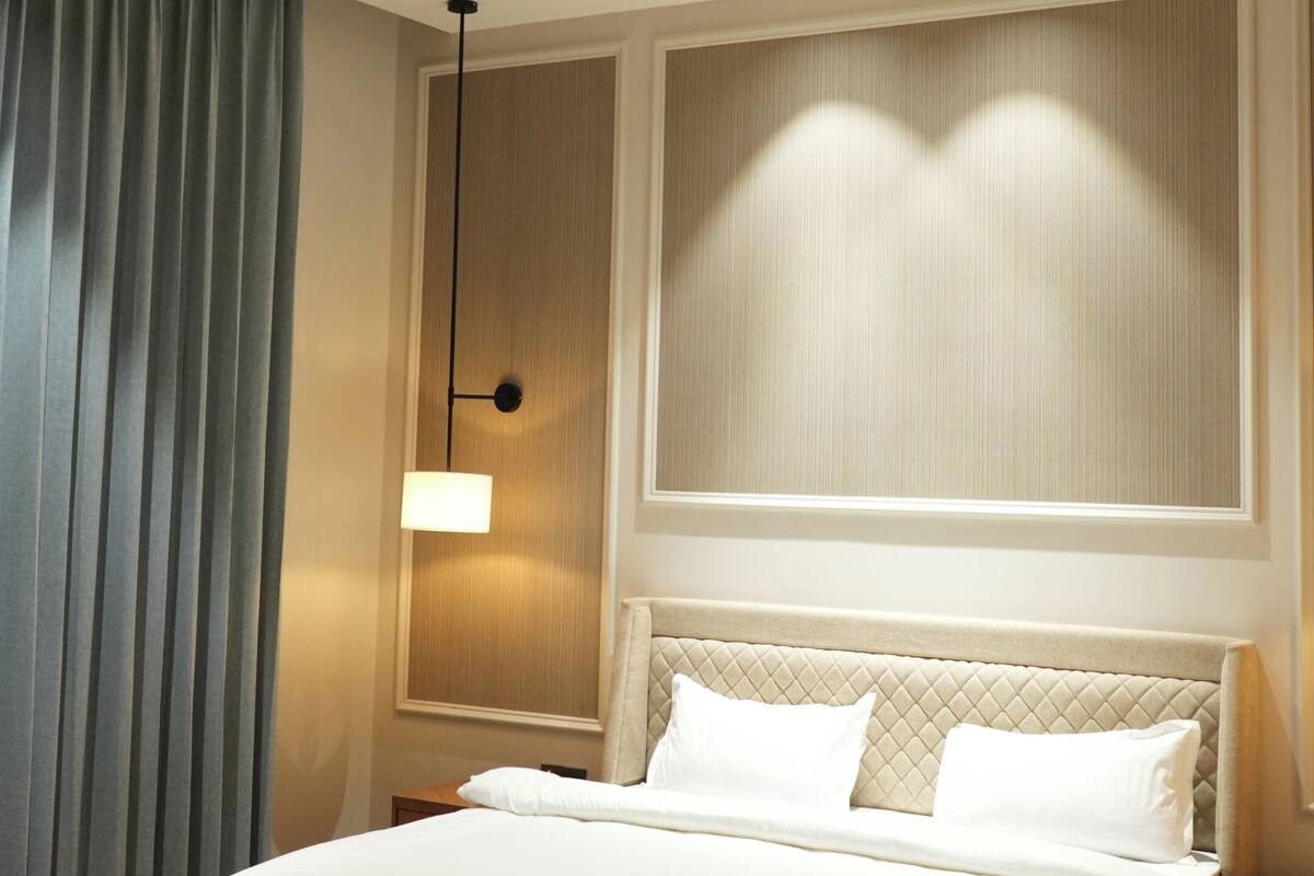 Quarto de hotel com cama, ventoinha no teto, luminária na parede e janela com cortinas.