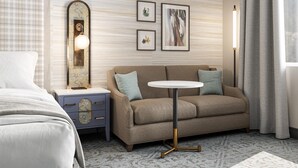 Quarto com cama, sofá, mesa de cabeceira, abajur e quadros na parede.
