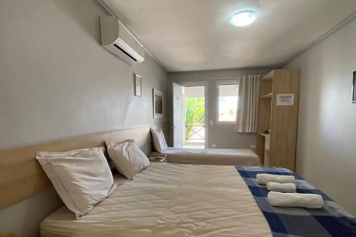 Quarto de hotel com cama, mesa de cabeceira, guarda-roupa e janela com cortinas.