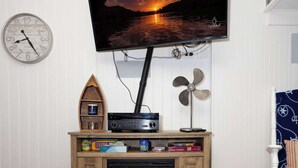 Uma sala de estar com televisão de tela plana montada acima de um móvel de madeira, um relógio na parede e um ventilador.