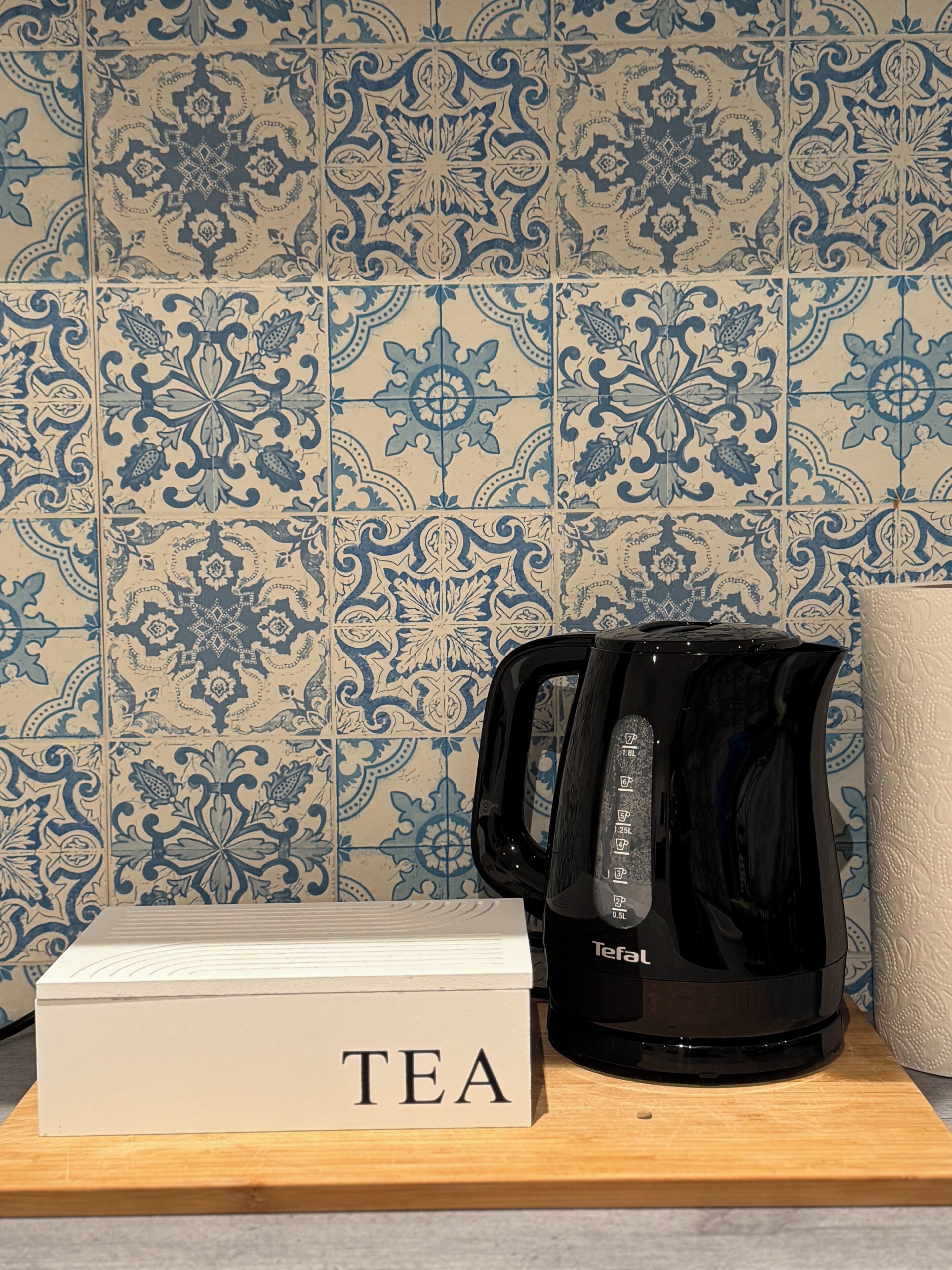 Uma cafeteira preta sobre uma superfície de madeira, com uma caixa identificada com a inscrição 'TEA' na frente.