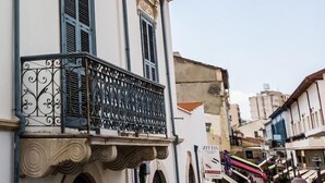 Vista da rua com um edifício com varanda e balaústres metálicos ornamentados, em estilo arquitetônico clássico.