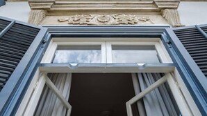 Entrada de um edifício com cornija decorativa, janela com persianas e ventoinha.