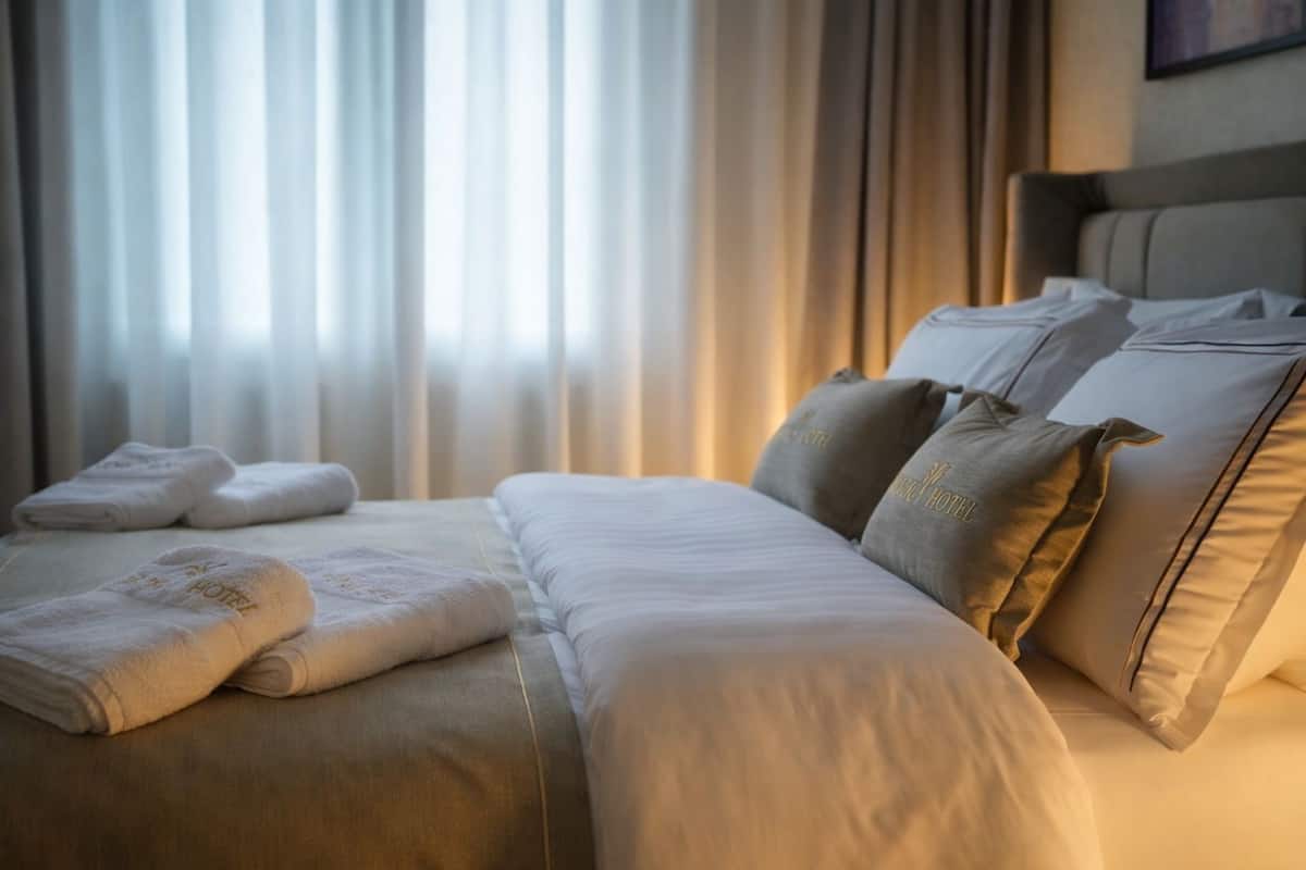 Quarto de hotel com cama, almofadas e toalhas dobradas.