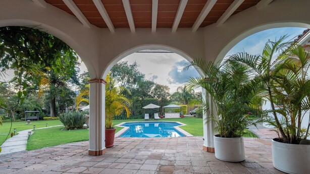 Área externa coberta com piscina, plantas em vasos e vista para um jardim.