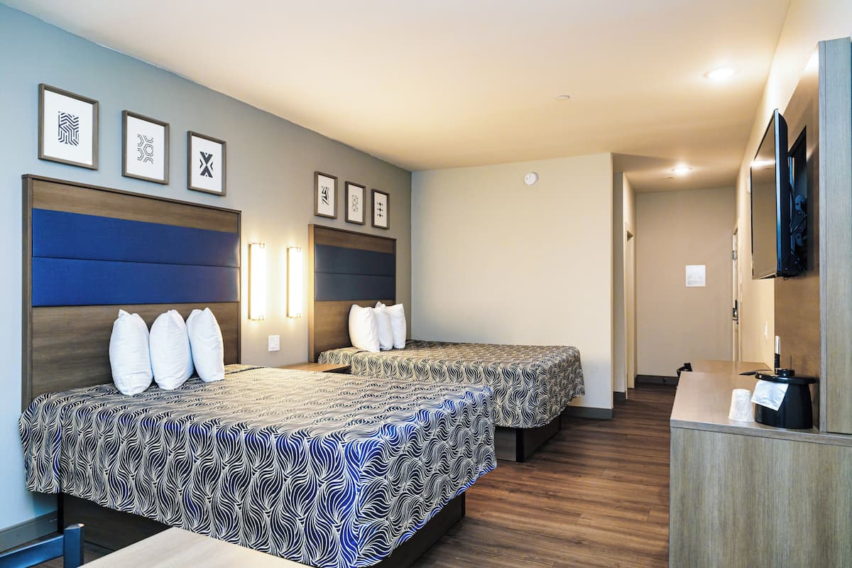 Quarto de hotel com duas camas, uma escrivaninha, televisão de tela plana e quadros na parede.