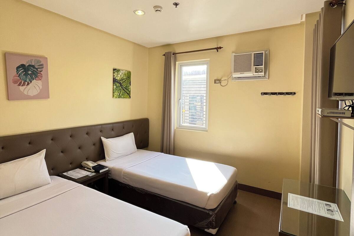Quarto de hotel com duas camas, uma televisão de tela plana, aparelho de ar condicionado e janela com persianas.