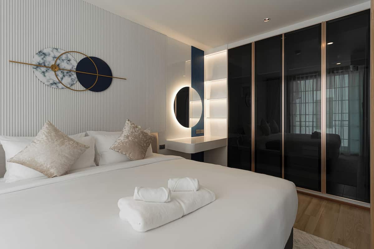 Quarto de hotel moderno com uma cama grande, mesa de cabeceira com espelho e guarda-roupa com portas deslizantes.