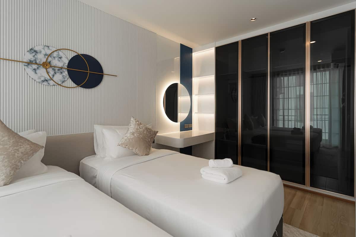 Quarto de hotel moderno com duas camas, um espelho grande, um relógio de parede e uma porta de armário deslizante.