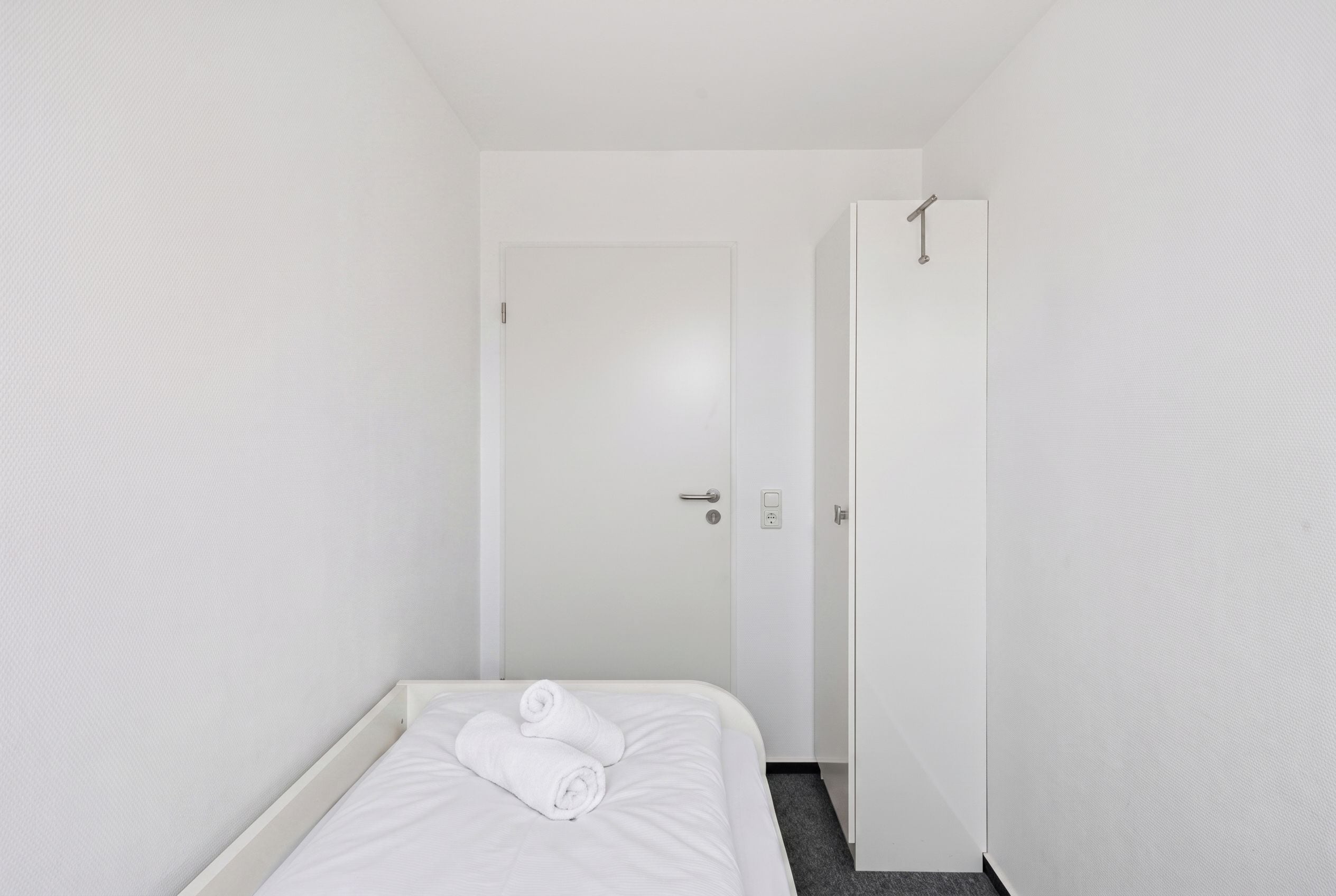Quarto pequeno, com uma cama de solteiro, porta e armário.