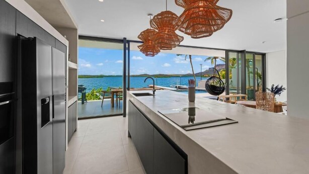 Cozinha moderna com uma ilha grande, vista para o mar e área de refeições com mesas ao ar livre.