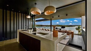 Cozinha moderna com uma ilha grande, área de jantar vista para a água, e sala de estar com vista.