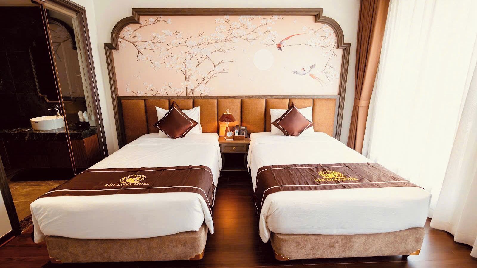 Quarto de hotel com duas camas, uma mesa de cabeceira, relógio fixado na parede e um painel decorativo.