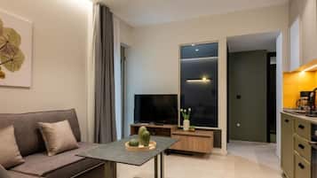 Uma sala de estar moderna com um sofá, uma mesa de centro, uma TV de tela plana e uma área de cozinha com armários e uma máquina de café.