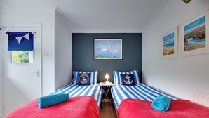 Quarto com duas camas, uma mesinha com abajur, um mapa emoldurado na parede e uma janela com cortina.