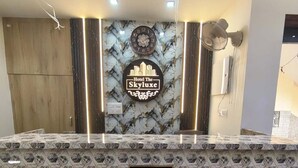 Balcão de recepção com parede estampada em mármore, um relógio e o logotipo do 'Hotel The Skyluxe'.
