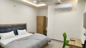 Quarto com cama, escrivaninha, cadeira, guarda-roupa, ventoinha no teto e aparelho de ar condicionado.