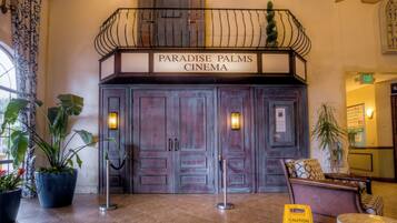 Entrada do Cinema Paradise Palms, com uma placa acima das portas, plantas em vasos e um aviso no chão.