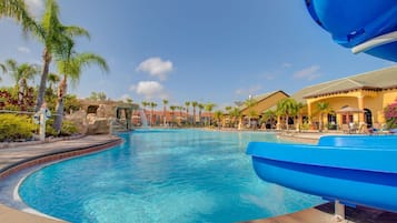Uma piscina com escorregador, palmeiras e um edifício com fachada amarela.