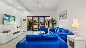 Uma sala de estar moderna com um sofá azul, um móvel para aparelhos eletrônicos branco e um ventilador de teto.