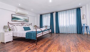 Quarto com cama, mesa de cabeceira, abajur, cadeira e janela com cortinas.