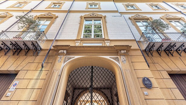 Fachada de prédio com uma grande entrada em arco, molduras de janelas ornamentadas e uma placa indicando um hotel.