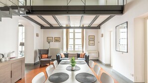 Uma sala de jantar espaçosa com teto alto, uma planta central e vista para a cidade através de grandes janelas.