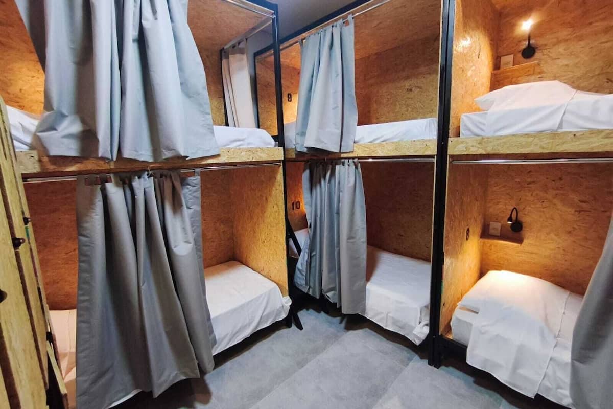 Quarto com beliche, paredes de madeira e uma pequena estante com abajur.