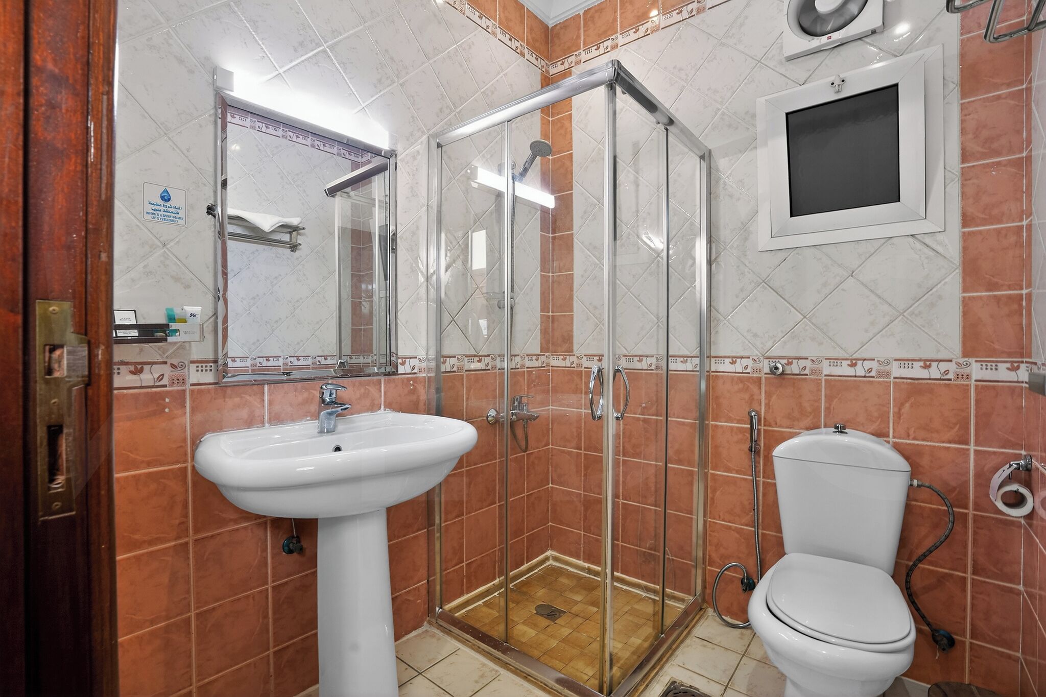 Casa de banho com cabine de duche envidraçada, lavatório branco e sanita.