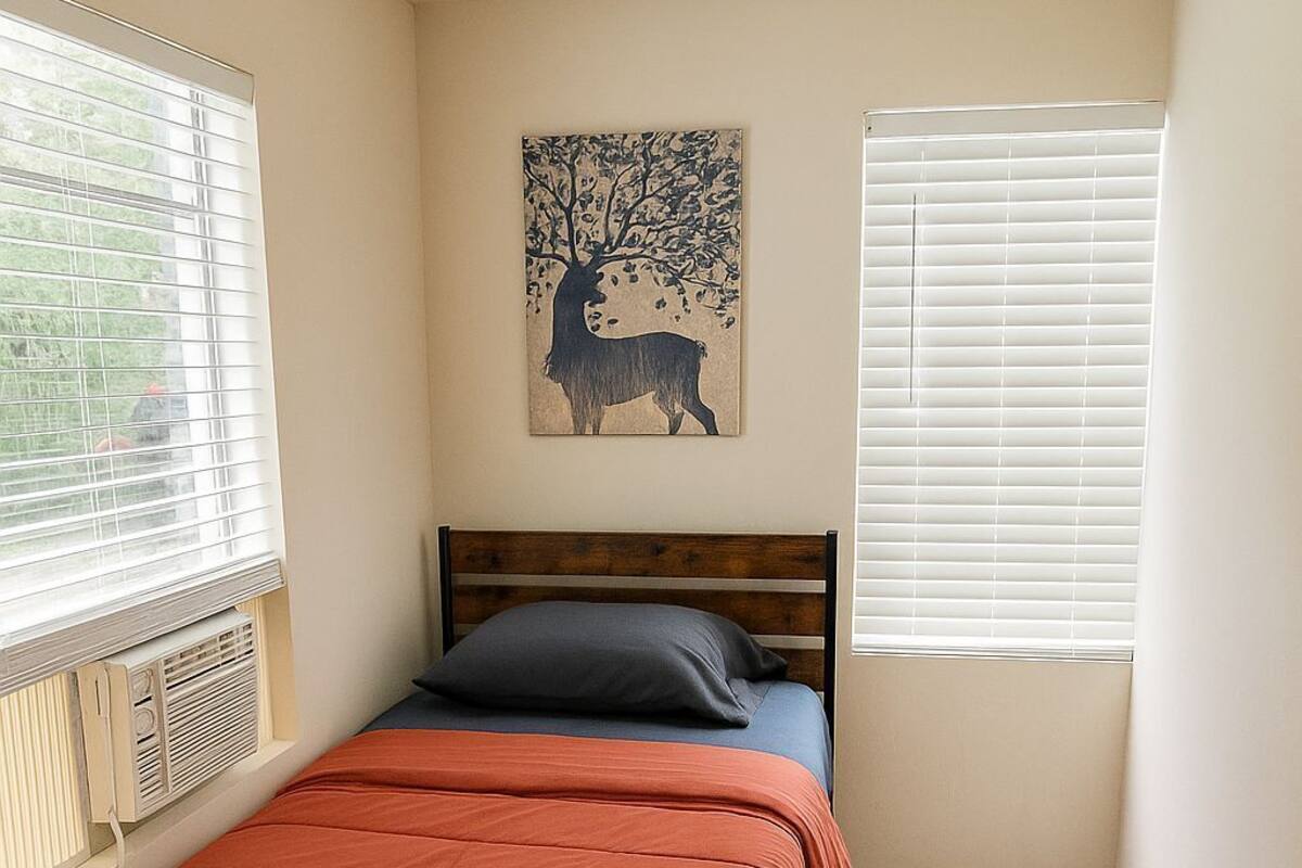 Quarto com cama, radiador, janela com persianas e uma obra de arte na parede.