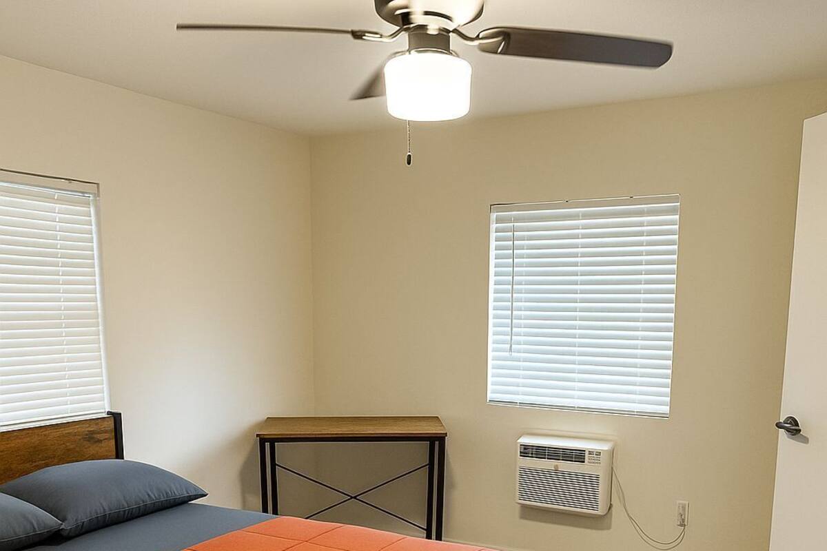 Quarto com cama, ventoinha no teto, janela e ar condicionado.